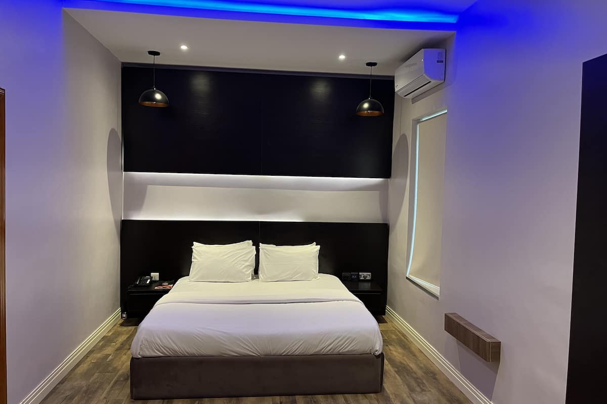 Quarto moderno com cama grande, cabeceira escura e iluminação ambiente azul.