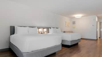 Quarto de hotel com duas camas, piso de madeira e luminária fixada na parede.
