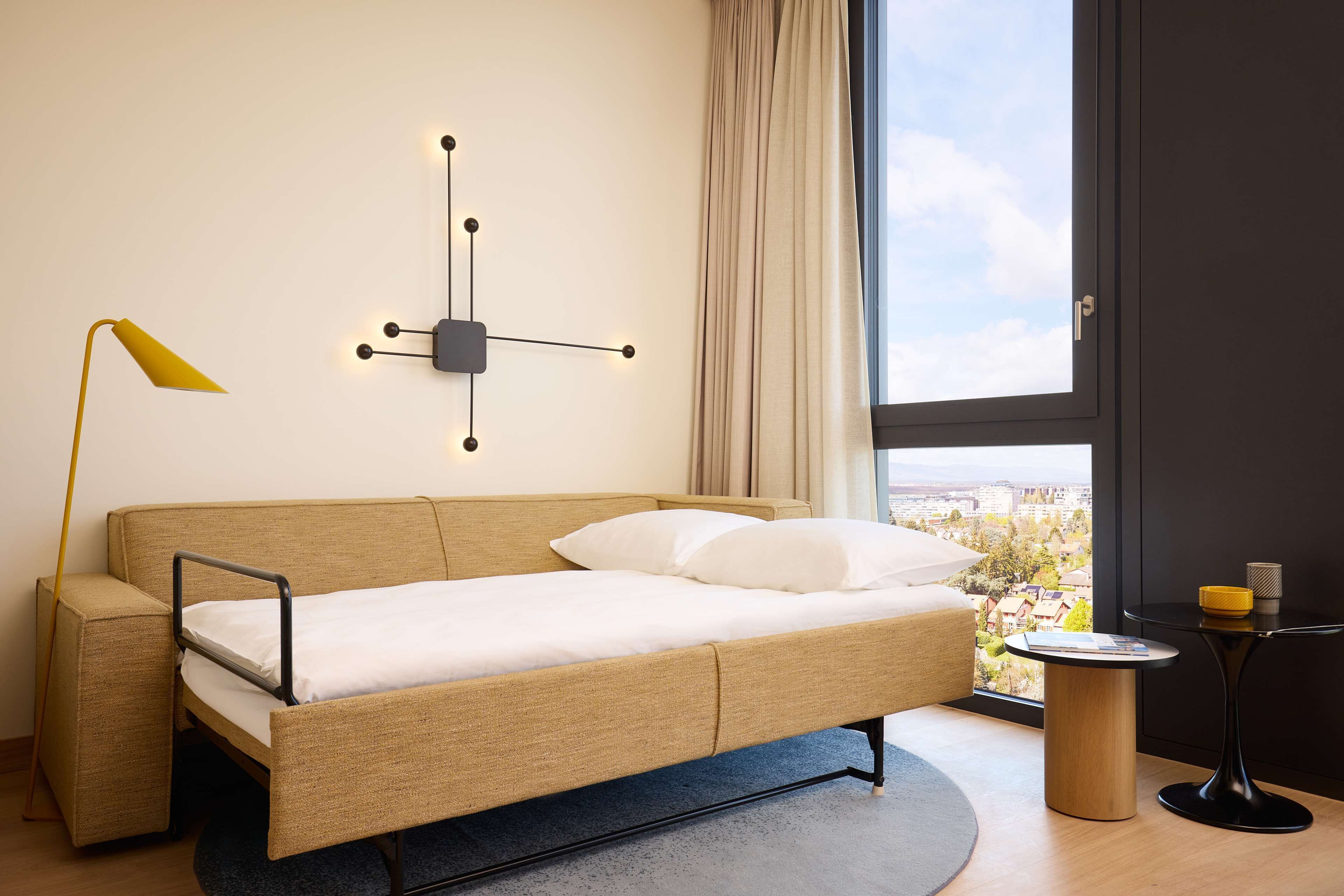 Quarto moderno com cama, mesa de cabeceira, luminária e arandela.