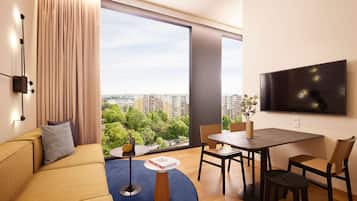 Uma sala de estar moderna com sofá, mesa de centro, mesa de jantar com cadeiras, TV de tela plana na parede e uma grande janela com vista para a cidade.