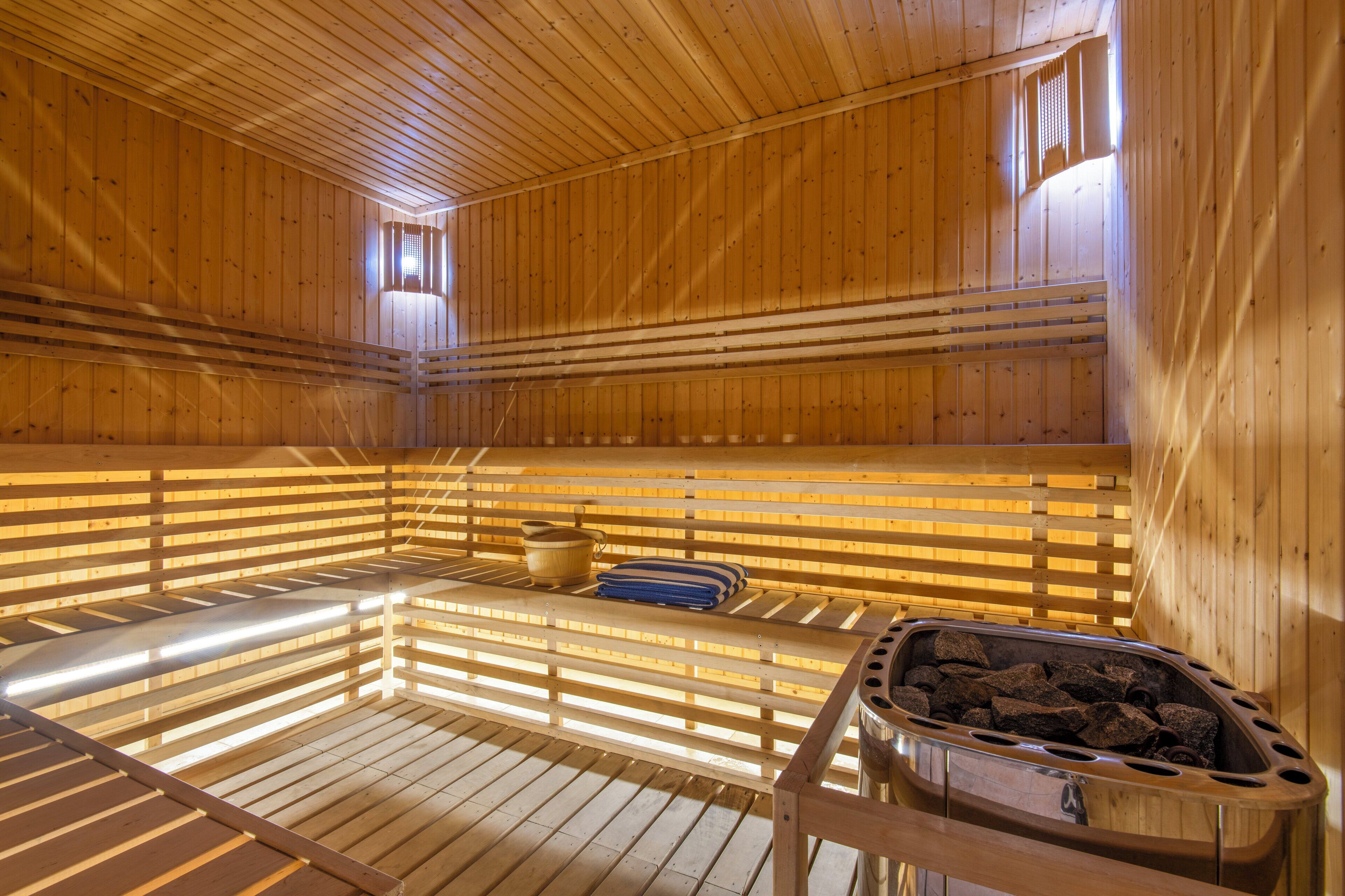 Uma sauna com paredes e bancos de madeira, um banco com uma toalha, e um recipiente com pedras.