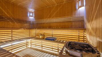 Uma sauna com paredes e bancos de madeira, um banco com uma toalha, e um recipiente com pedras.