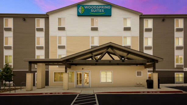 Um hotel com telhado plano, entrada coberta e uma placa com a inscrição "Woodspring Suites".