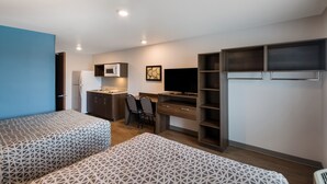 Quarto compacto com duas camas, uma escrivaninha, televisão e cozinha compacta.