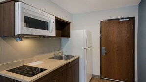 Cozinha compacta com micro-ondas, pia e geladeira, armários de madeira e uma porta.
