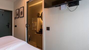 Quarto de hotel com cama, porta, espelho e televisão presa à parede.