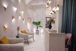 Uma área de recepção moderna com parede de mármore, balcão de recepção e dois sofás com almofadas amarelas.