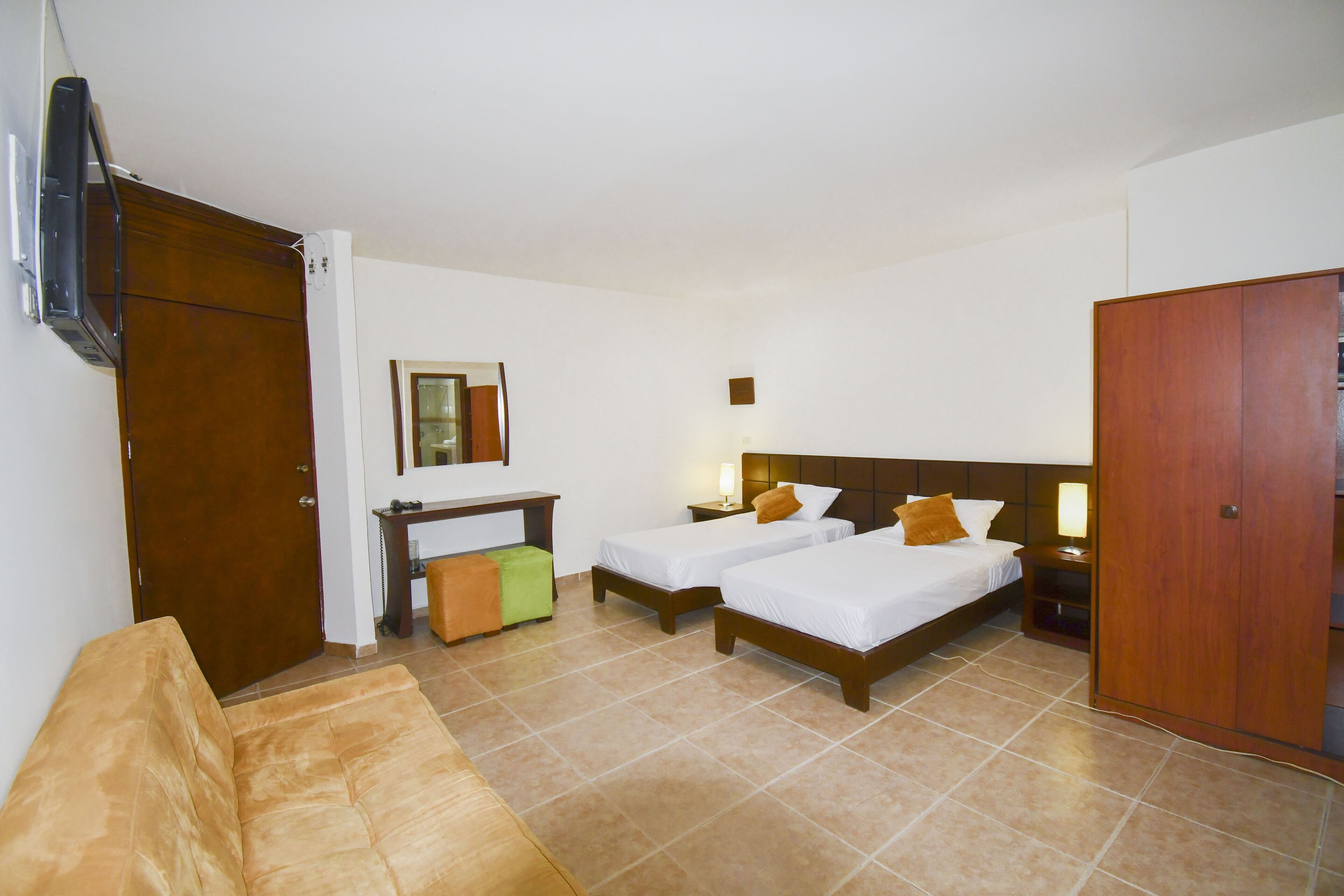 Quarto de hotel com duas camas, um sofá, uma televisão, uma escrivaninha e um guarda-roupa.