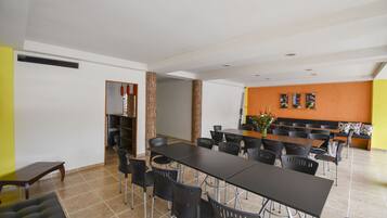 Uma sala de jantar ampla, com uma mesa comprida e várias cadeiras, um sofá, e uma pequena área de cozinha ao fundo.