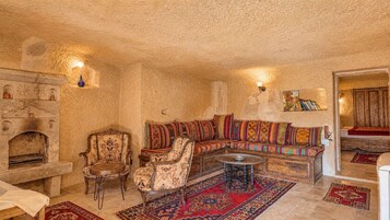 Um quarto tradicional com paredes de pedra, lareira, sofá com almofadas coloridas, uma cadeira de madeira e uma pequena mesa.