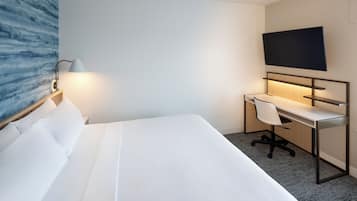 Quarto de hotel com cama, escrivaninha, cadeira, televisão e abajur.
