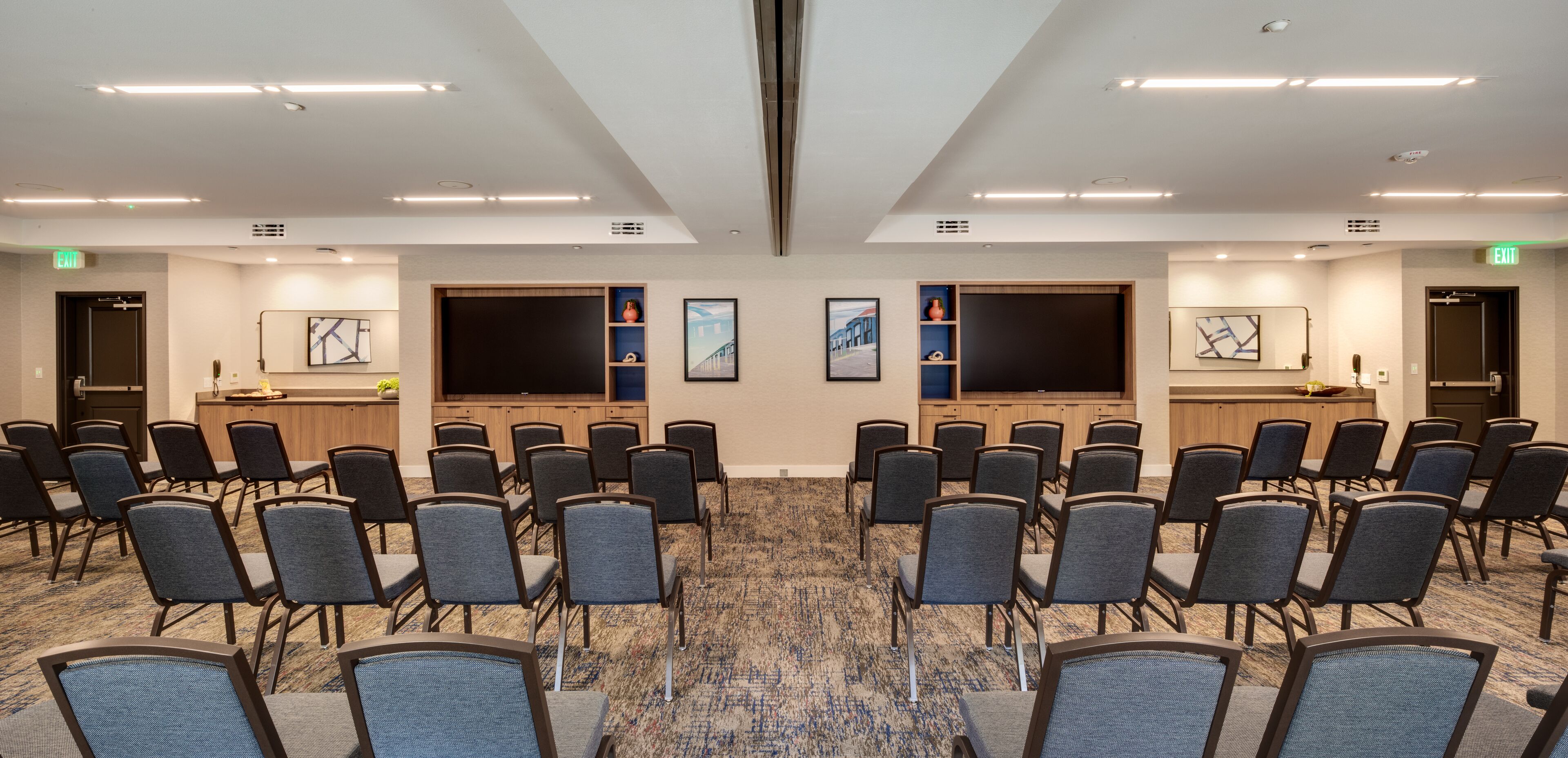 Sala de conferências com fileiras de cadeiras, um púlpito e duas telas grandes nas paredes.
