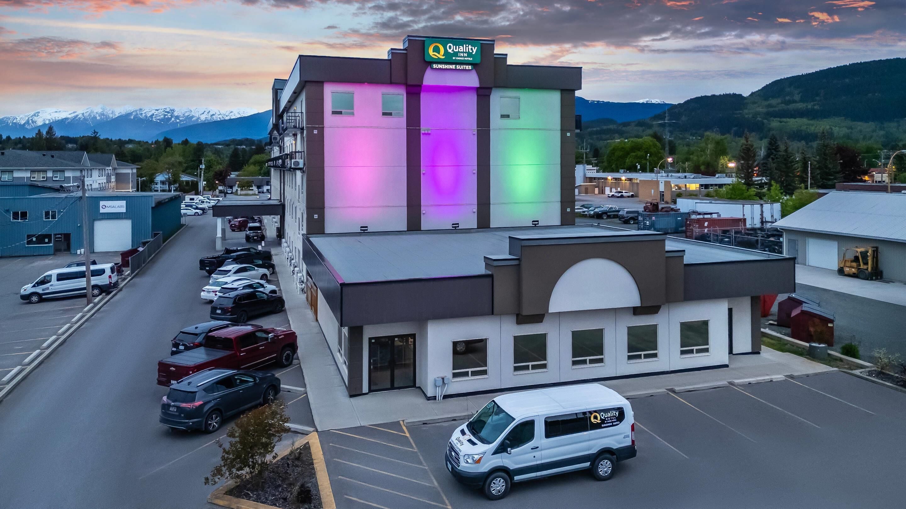 Hotel com design moderno, estacionamento e vista para montanhas ao fundo.