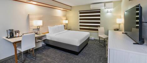 Quarto de hotel moderno com cama, escrivaninha, cadeira e televisão.