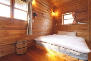 Quarto de cabana de madeira com uma cama, uma janela, uma cortina e um barril de madeira.