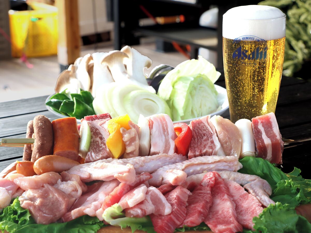 Uma refeição com diversos tipos de carne, legumes e um copo de cerveja sobre uma mesa de madeira.