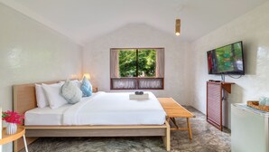 Quarto com cama, janela com cortinas, televisão e uma pequena mesa com abajur.