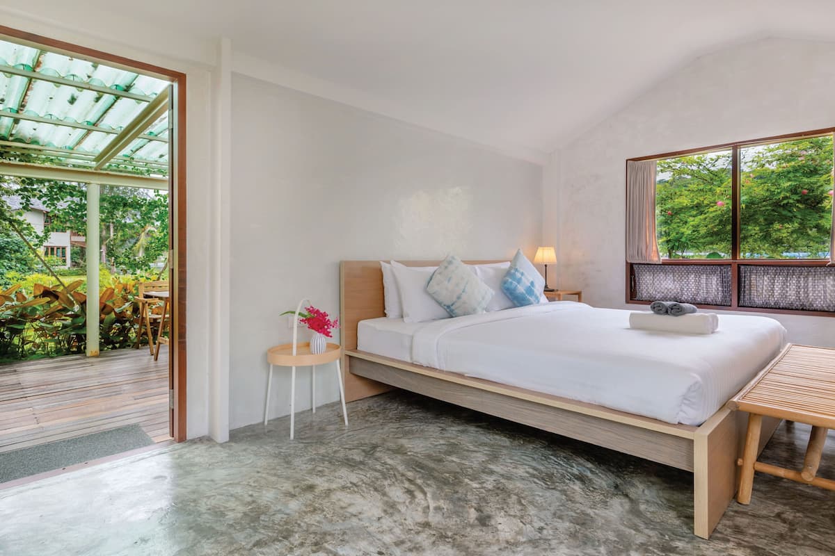 Quarto com cama, mesa de cabeceira e janela com vista para o verde.
