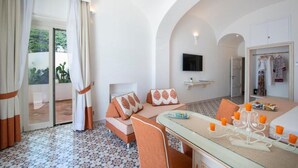 Quarto de hotel com sofá, mesa de jantar e velas, e uma televisão.