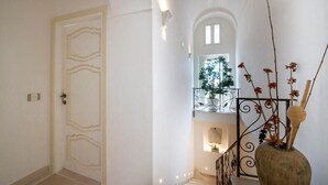 Um corredor com uma porta branca, uma escada com corrimão e um vaso decorativo com galhos.