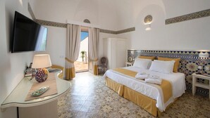 Quarto de hotel com uma cama, televisão, escrivaninha com abajur e vista para o exterior.