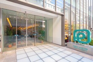 Entrada moderna de hotel com portas de vidro, plantas em vasos e placa indicando o Prince Smart Inn em Osaka.