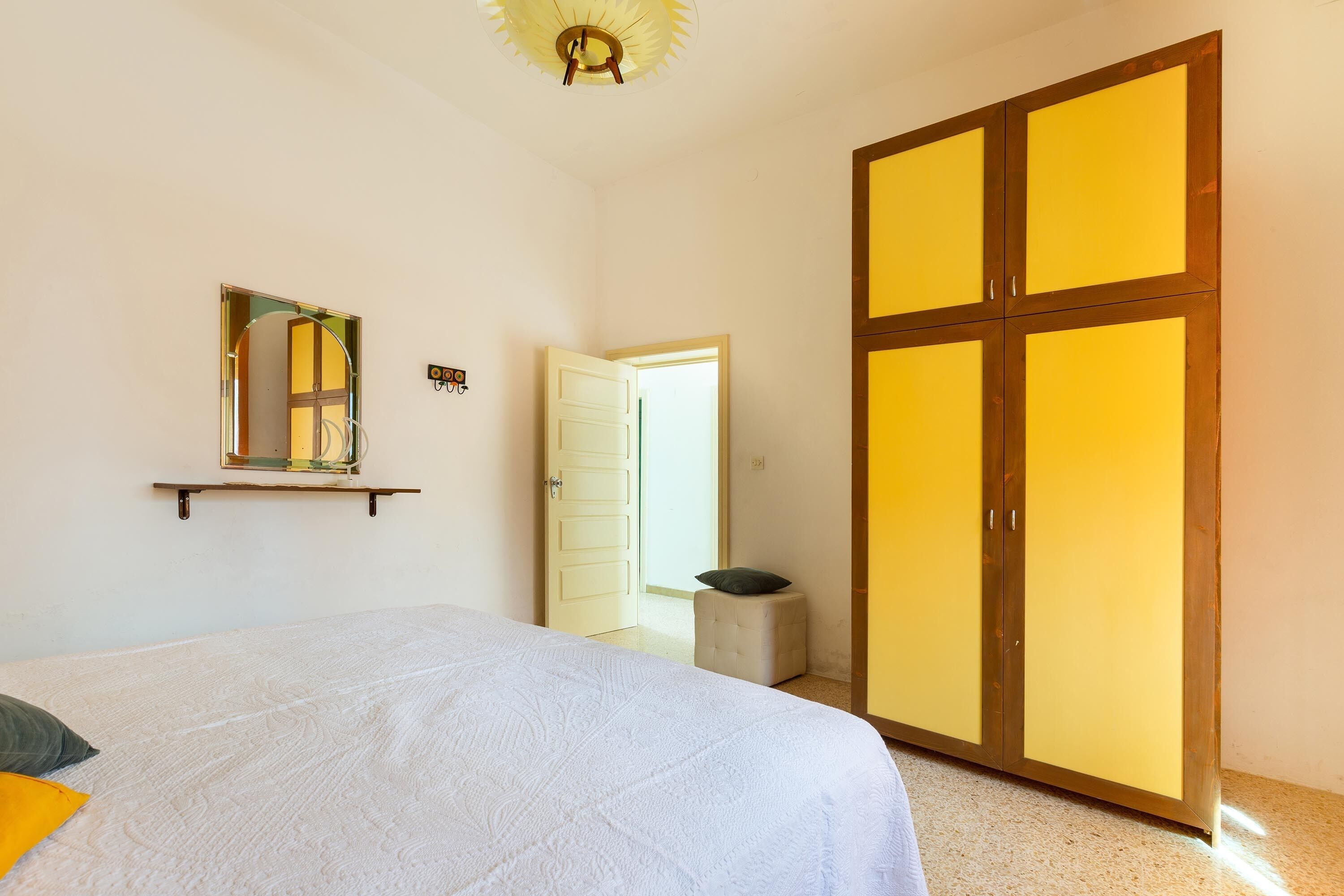 Quarto com cama, guarda-roupa, espelho e porta que dá para outro cômodo.