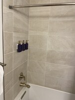 Casa de banho com azulejos bege, uma banheira, zona de duche e dois dispensadores de sabonete líquido fixados na parede.
