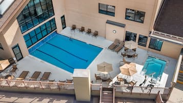 Área de piscina no terraço com várias espreguiçadeiras e guarda-sóis, cercada por um deck de madeira e um parapeito de vidro.