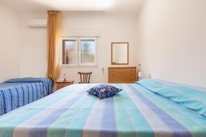 Quarto com duas camas, uma janela com cortinas, cômoda de madeira e um espelho.