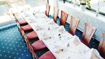 Uma sala de jantar com uma mesa comprida posta para refeição, cadeiras de madeira e vista para o exterior através de grandes janelas.