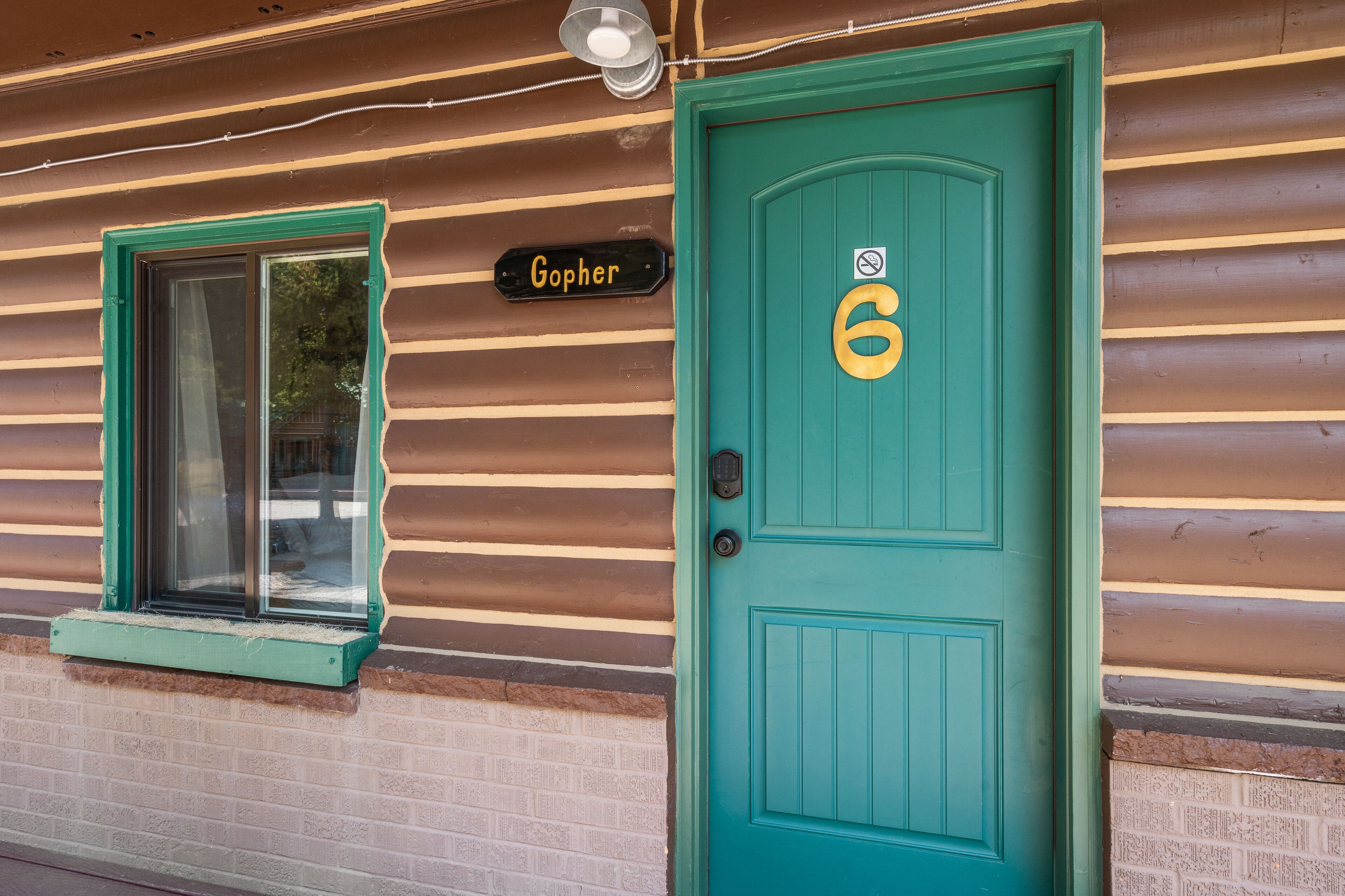 Uma porta azul-esverdeada com o número 6, uma janela com moldura verde e uma placa com a inscrição 'Gopher'.