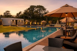 Piscina com espreguiçadeiras e guarda-sóis, cercada por um jardim ajardinado e um edifício com iluminação externa.