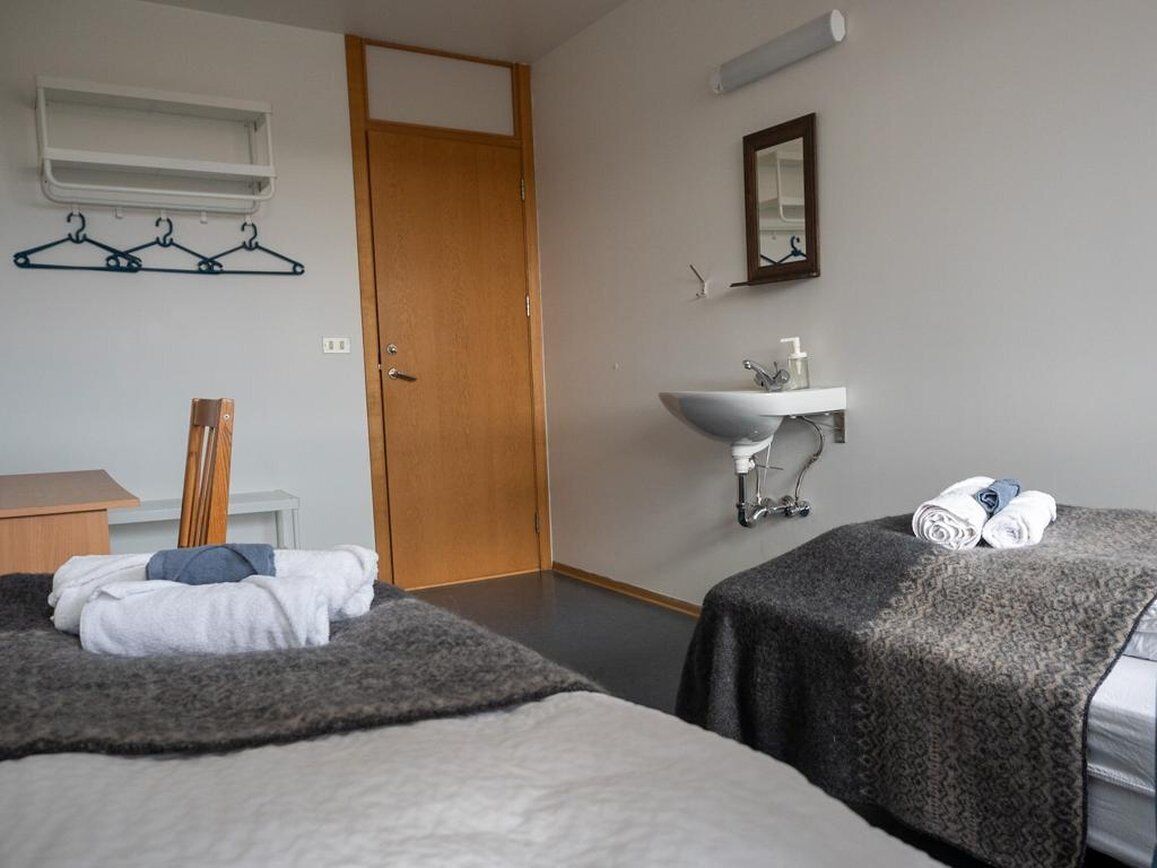 Quarto de hotel com duas camas, porta de madeira, pia branca e espelho.