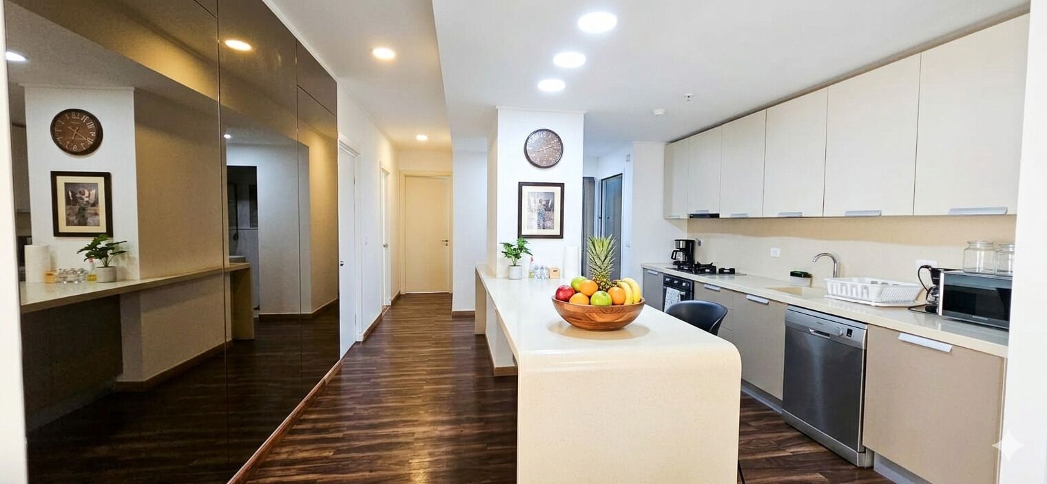 Uma cozinha moderna com armários brancos, uma ilha central com uma fruteira e piso de madeira.