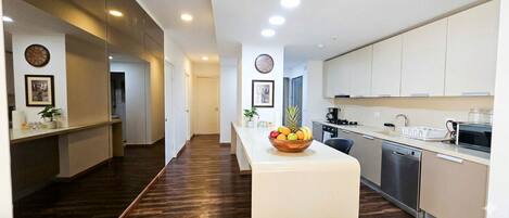 Uma cozinha moderna com armários brancos, uma ilha central com uma fruteira e piso de madeira.