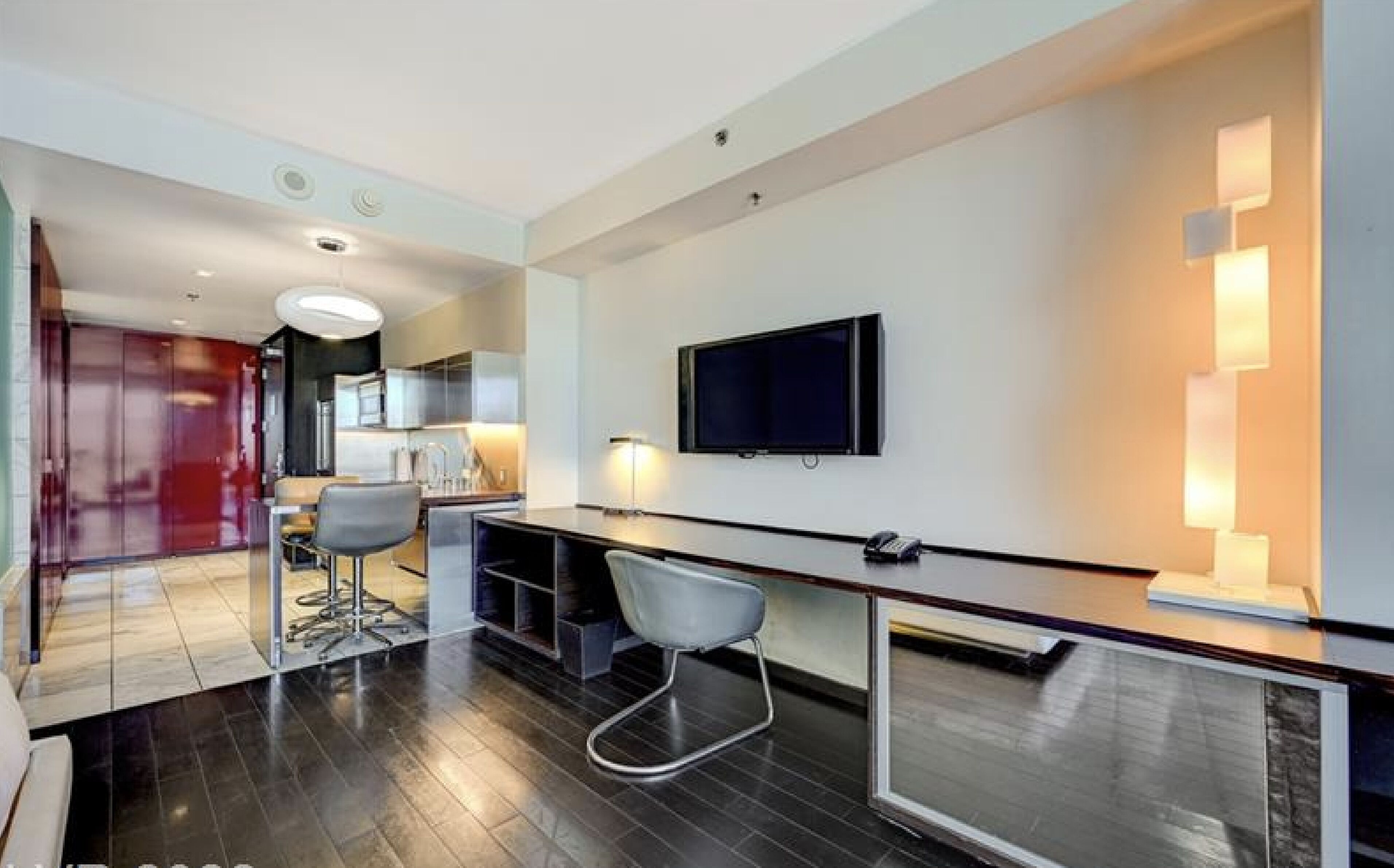 Quarto de hotel moderno com cozinha, mesa de jantar e televisão na parede.