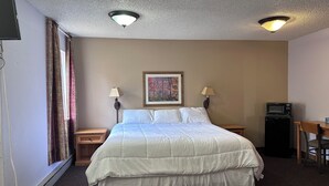 Quarto de hotel com uma cama grande, duas luminárias de cabeceira, um quadro na parede, uma escrivaninha com cadeira e um micro-ondas.