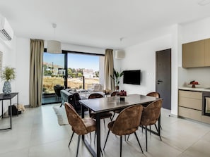 Uma zona de refeições moderna com uma mesa grande e cadeiras, uma televisão de ecrã plano na parede e vista para o exterior.