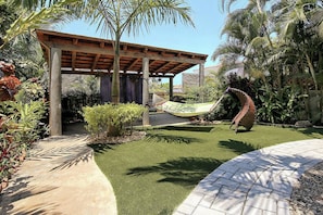 Um jardim com rede, pérgola e muro de pedra.