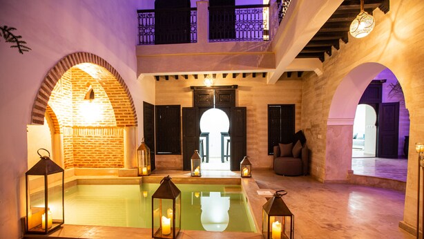Uma área de piscina interior luxuosa, com uma fonte central, rodeada por arcos e iluminada por lanternas.