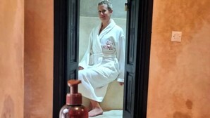 Uma pessoa vestida com um robe branco sentada num degrau de uma porta.