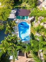 Vista aérea de um resort com piscina, cercada por palmeiras e um edifício com telhado vermelho.