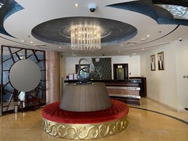 Um lobby moderno com uma mesa redonda central, um candelabro e um balcão de recepção.