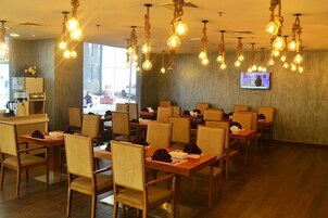 Um restaurante com várias mesas e cadeiras, luminárias pendentes e uma televisão na parede.