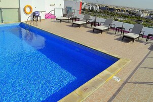 Piscina no terraço com água azul cristalina, rodeada por espreguiçadeiras e um salva-vidas.