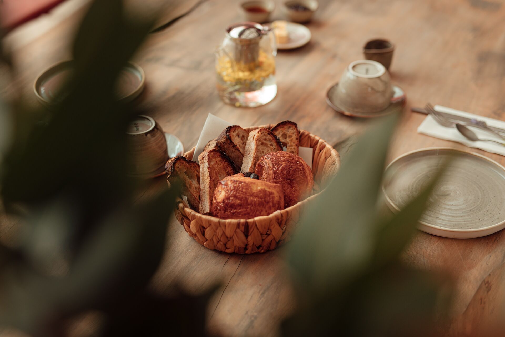 Uma mesa de madeira com uma cesta de pão, um pote de vidro e um prato.