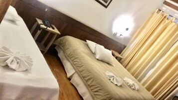 Quarto de hotel com duas camas, uma mesinha com telefone e uma luminária fixada na parede.