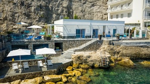 Um hotel à beira-mar com área de piscina, espaço para sentar ao ar livre e escadaria que dá acesso ao edifício.