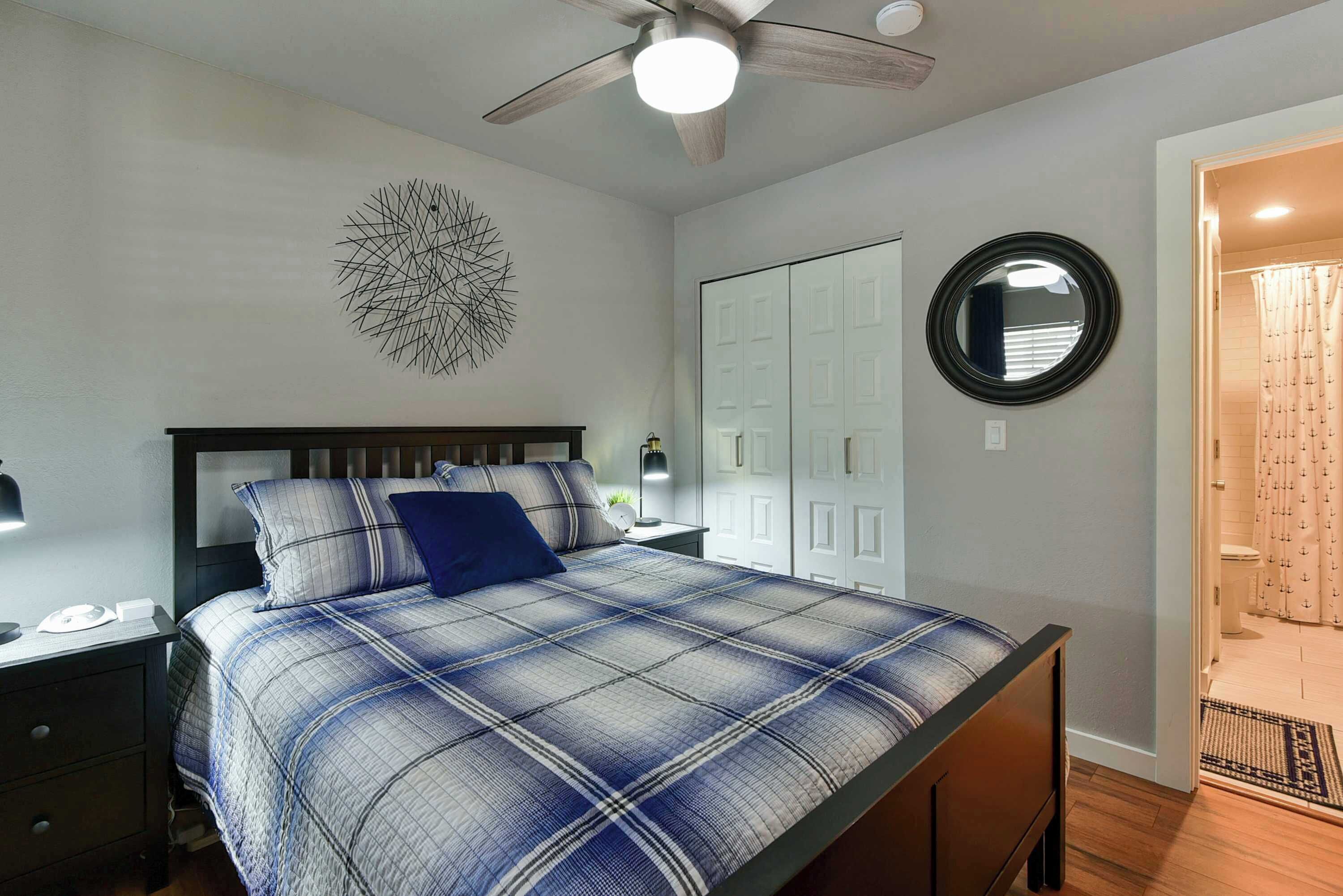 Quarto com cama, mesa de cabeceira, decoração na parede, guarda-roupa e ventilador de teto.